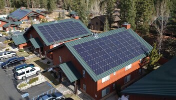 Um edifício com painéis solares no telhado, rodeado por árvores e outros edifícios.