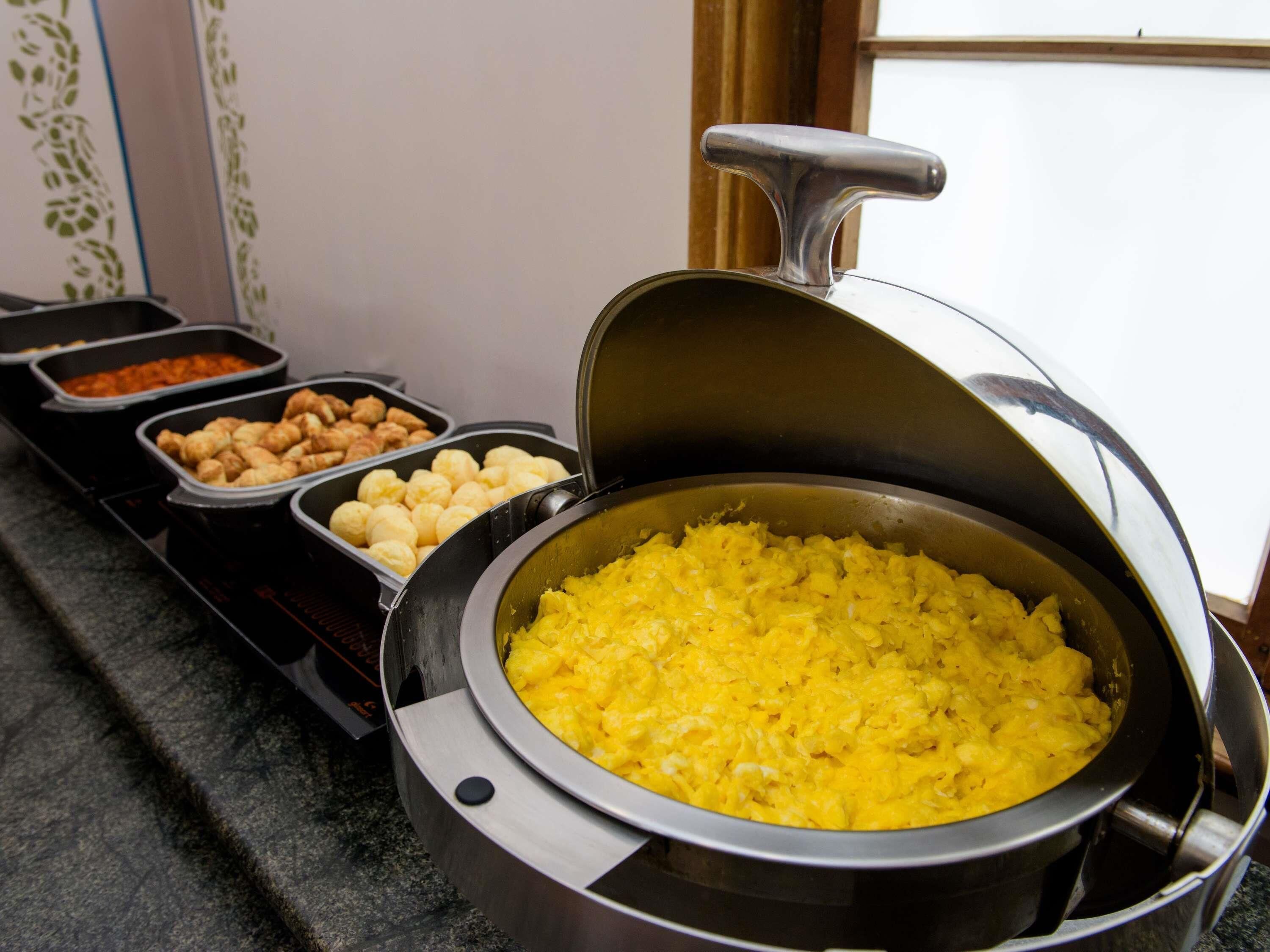 Buffet com diversos alimentos, incluindo uma grande panela de ovos mexidos.