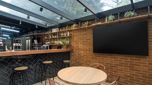 Uma área de bar moderna com mesa de madeira e banquetas, uma parede de tijolos e uma televisão de tela plana grande.