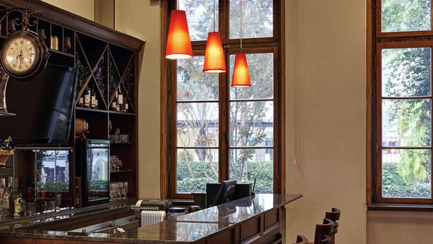 Uma área de bar com balcão de madeira, prateleiras com garrafas e luminárias pendentes laranjas.