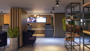 Um lobby moderno com balcão de recepção, área de estar e uma tela de televisão.