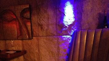Restaurante com iluminação fraca, parede de mármore, mesa de madeira com um prato e um copo, e uma cadeira.