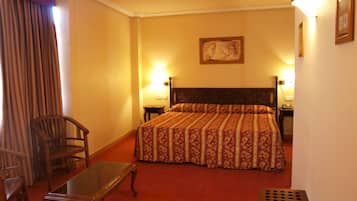Quarto de hotel com uma cama, duas mesas de cabeceira, uma cadeira e uma pequena mesa.