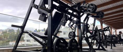 Uma academia com diversos equipamentos de musculação, incluindo bancos e halteres, sob um teto de madeira.