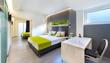 Quarto de hotel moderno com uma cama grande, uma escrivaninha e uma cadeira. Há uma janela com vista para o verde lá fora.