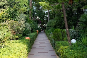 Um caminho bordeado por sebes e árvores bem aparadas, serpenteando por um jardim exuberante.