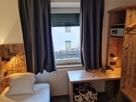 Quarto com cama, escrivaninha, radiador, janela com cortinas e parede com um aviso.
