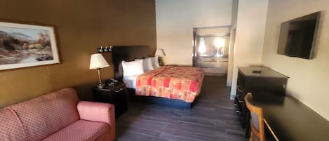 Quarto de hotel com cama, escrivaninha, cadeira, sofá, luminária, telefone e um quadro na parede.