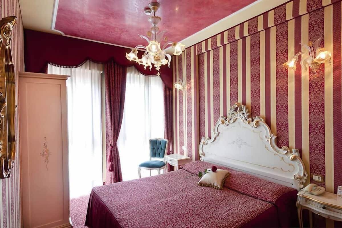 Quarto com cama grande, lustre, penteadeira com espelho e papel de parede listrado.