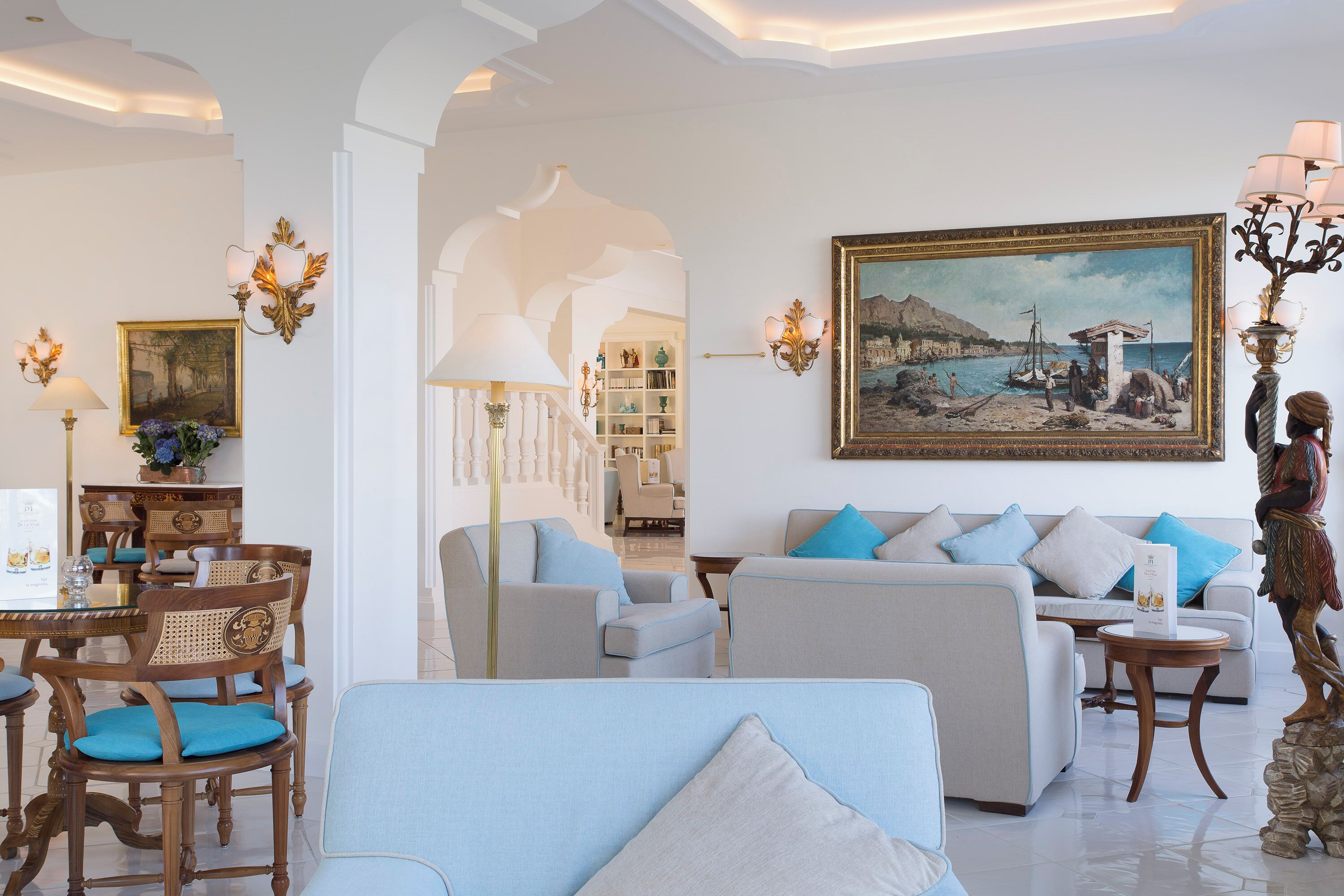 Sala de estar bem iluminada com área de jantar, sofás e uma pintura de paisagem costeira.