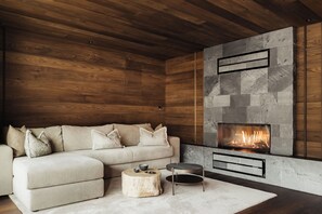 Uma sala de estar moderna com lareira de pedra, teto de madeira e sofá bege.