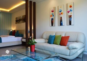 Uma sala de estar moderna com um sofá, uma mesa de centro de vidro e uma planta em vaso. Há três quadros na parede retratando flores.