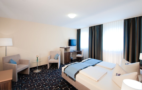 Quarto de hotel com uma cama, uma mesa, uma cadeira, uma TV e uma pequena mesa com um vaso.