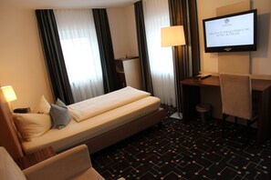 Quarto de hotel com cama, escrivaninha, cadeira e televisão exibindo uma mensagem de boas-vindas.
