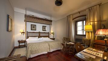 Quarto de hotel com uma cama grande, uma escrivaninha, uma cadeira, uma janela e um ventilador de teto.
