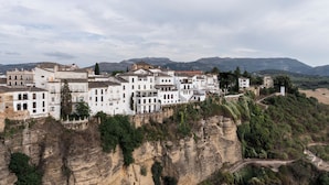 Um complexo de edifícios brancos empoleirado em um penhasco, com montanhas ao fundo.