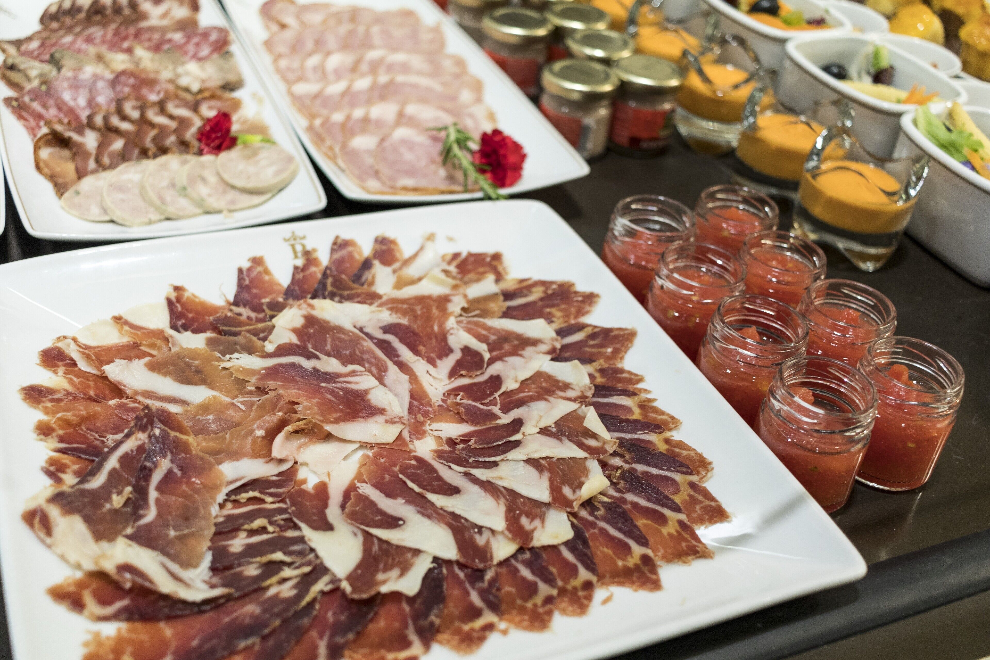 Buffet com diversos alimentos, incluindo fatias de carne e pequenos potes de molhos.