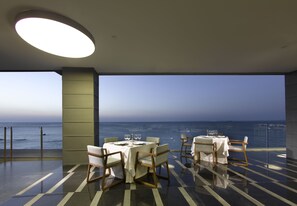 Uma área de refeições com vista para o mar, com uma mesa posta para dois e cadeiras.