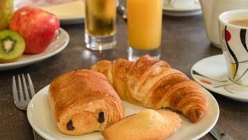 Mesa de café da manhã com croissants, uma travessa de frutas, um copo de suco e uma xícara de café.