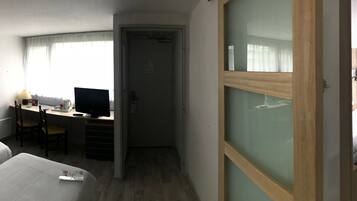 Quarto de hotel com duas camas, uma mesa com computador e vista para o mar através de uma janela.