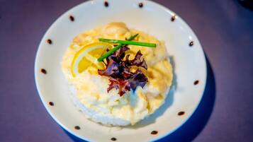 Um prato de comida com base cremosa, coberto com uma fatia de limão e cebolinha picada, e decorado com uma folha de alface roxa.