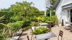 Um pátio com mesa e cadeiras, uma piscina pequena e muita vegetação.