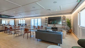 Uma sala de estar ampla com sofá, mesas de jantar e cadeiras, televisão de tela plana e lareira.