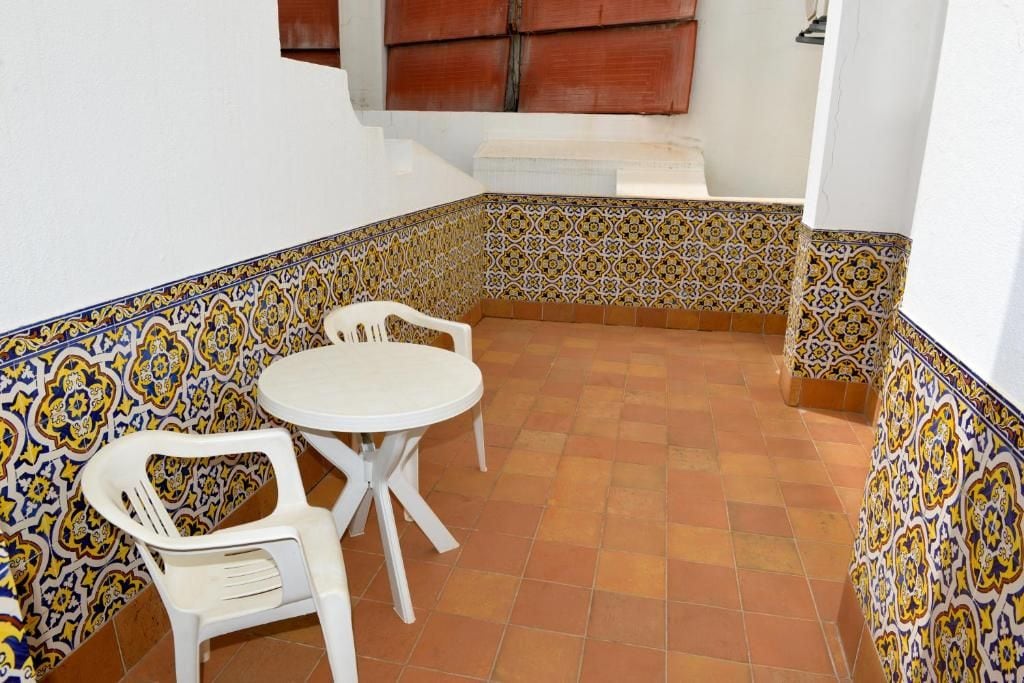 Uma pequena área de pátio com uma mesa redonda e duas cadeiras, cercada por azulejos estampados.
