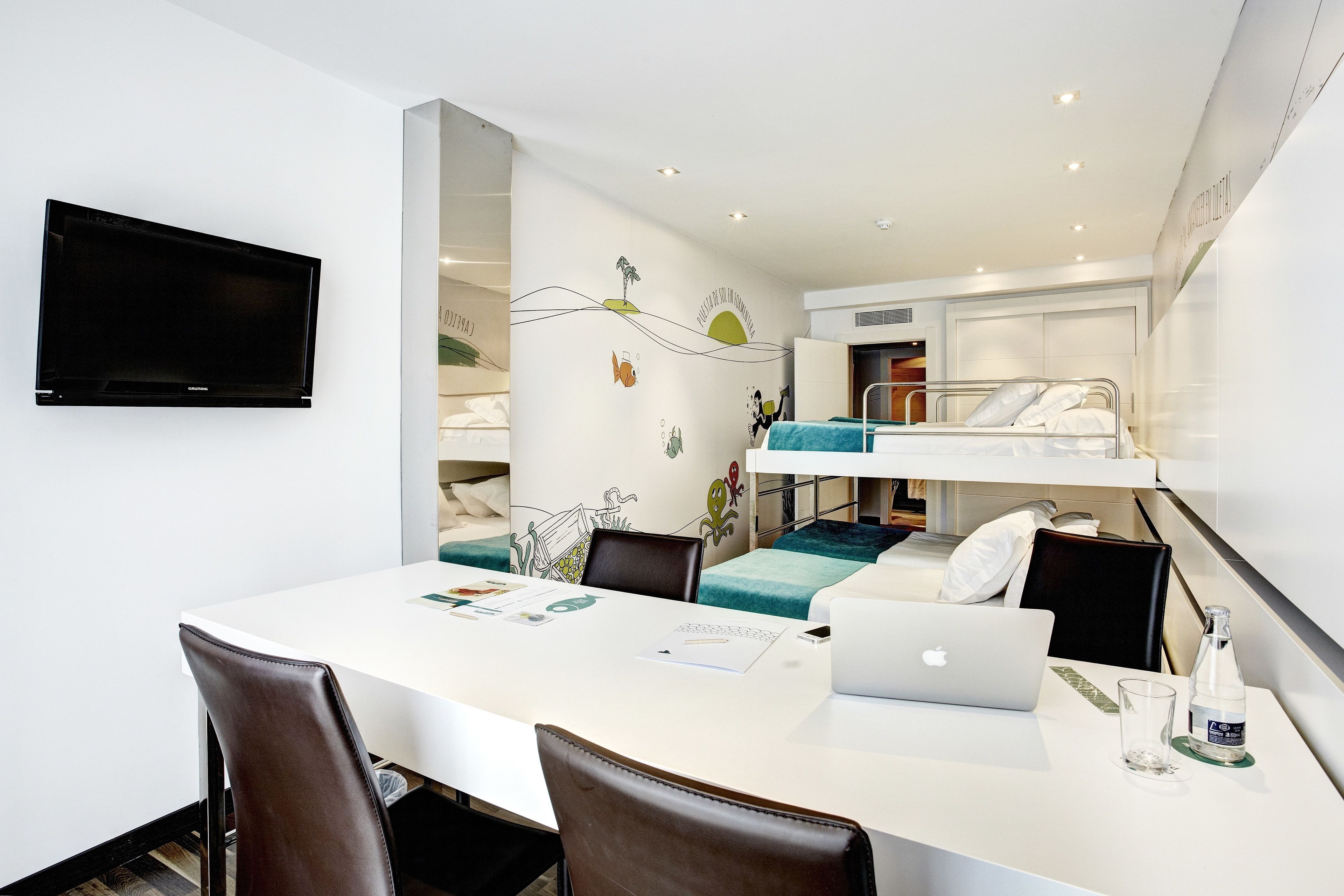 Quarto de hotel moderno com área de refeições, televisão de tela plana, beliche e cozinha compacta.