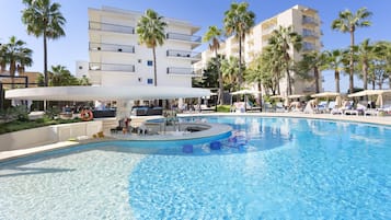Piscina com espreguiçadeiras e guarda-sóis, cercada por palmeiras e edifícios modernos.