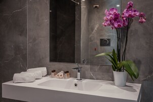 Casa de banho moderna com lavatório de mármore, toalhas brancas, uma orquídea em vaso e um espelho.