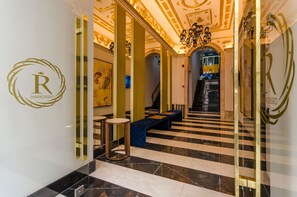 Um hall de hotel luxuoso com uma escadaria imponente, piso de mármore e decoração elegante.
