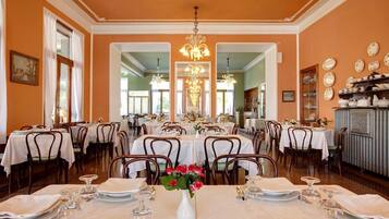Uma sala de jantar com várias mesas preparadas para o serviço, um lustre e um vaso de flores.