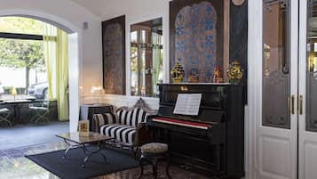 Um piano, um sofá e uma pequena mesa num quarto com paredes estampadas e uma porta com painéis de vidro decorativos.