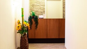Uma área de recepção com balcão de madeira, unidade de ar condicionado na parede e balcão de atendimento com uma planta verde.