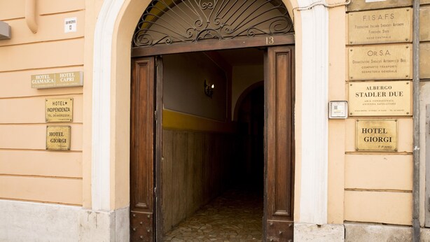 Entrada de hotel com chão de azulejos e porta de madeira.