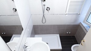 Casa de banho moderna com uma sanita branca, um bidé, um chuveiro e uma casa de toilette.