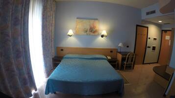 Quarto de hotel com uma cama, duas luminárias laterais, uma escrivaninha e uma cadeira.