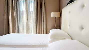 Quarto de hotel com uma cama grande, abajur e vista através de cortinas leves.
