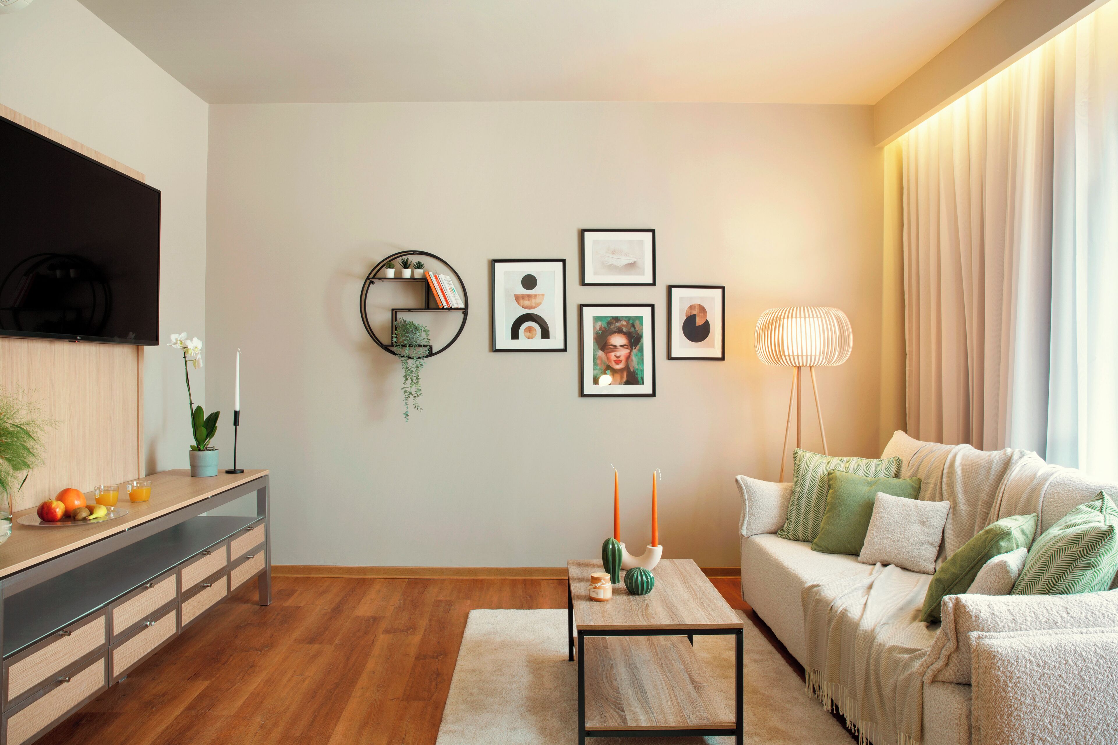 Uma sala de estar moderna com um sofá, mesa de centro e televisão presa na parede. Há quadros emoldurados e uma pequena estante com objetos decorativos.
