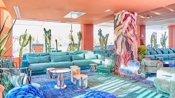 Uma sala de estar ampla com um sofá verde, tapetes com padrão azul e verde e uma grande escultura de cacto.