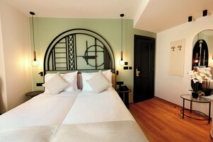 Cama de casal com cabeceira, mesas de cabeceira e uma pequena mesa redonda com um vaso de planta.