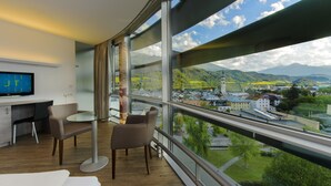 Quarto de hotel moderno com uma janela grande que oferece vista para uma cidade e montanhas.