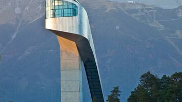Um edifício moderno com um design curvo singular, rodeado por uma floresta e montanhas ao fundo.