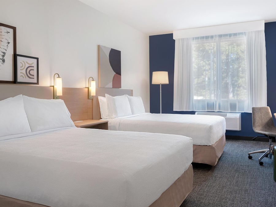 Quarto de hotel com duas camas, uma escrivaninha, uma cadeira e uma janela com cortinas.