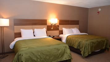 Quarto de hotel com duas camas, cada uma com colcha verde, mesa de cabeceira com abajur e luminária na parede.