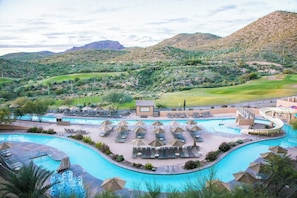Resort com várias piscinas, espreguiçadeiras e montanhas ao fundo.