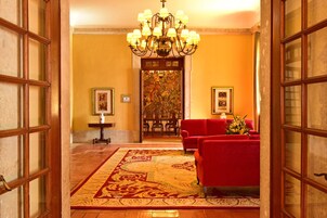 Um hall com um sofá vermelho, um candelabro e um tapete estampado.