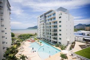 Um hotel moderno com uma grande área de piscina, várias varandas e vista para a praia.