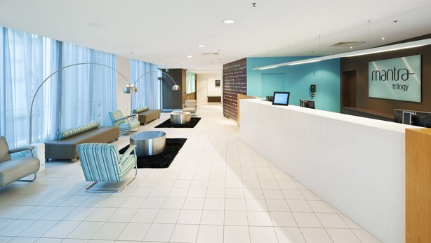 Uma área de recepção moderna, com balcão, espaço de estar e uma grande janela com cortinas.